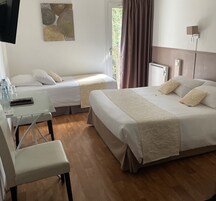 Quarto de hotel com duas camas de solteiro, uma mesa com cadeira, televisão presa na parede e janela com cortinas.