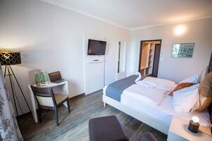 Quarto de hotel com cama, escrivaninha, cadeira e televisão fixada na parede.