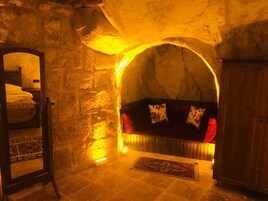 Quarto com paredes de pedra, uma cama, um armário de madeira e um sofá com almofadas florais.