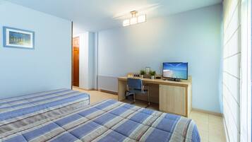 Quarto com duas camas, uma escrivaninha, uma cadeira e uma televisão.