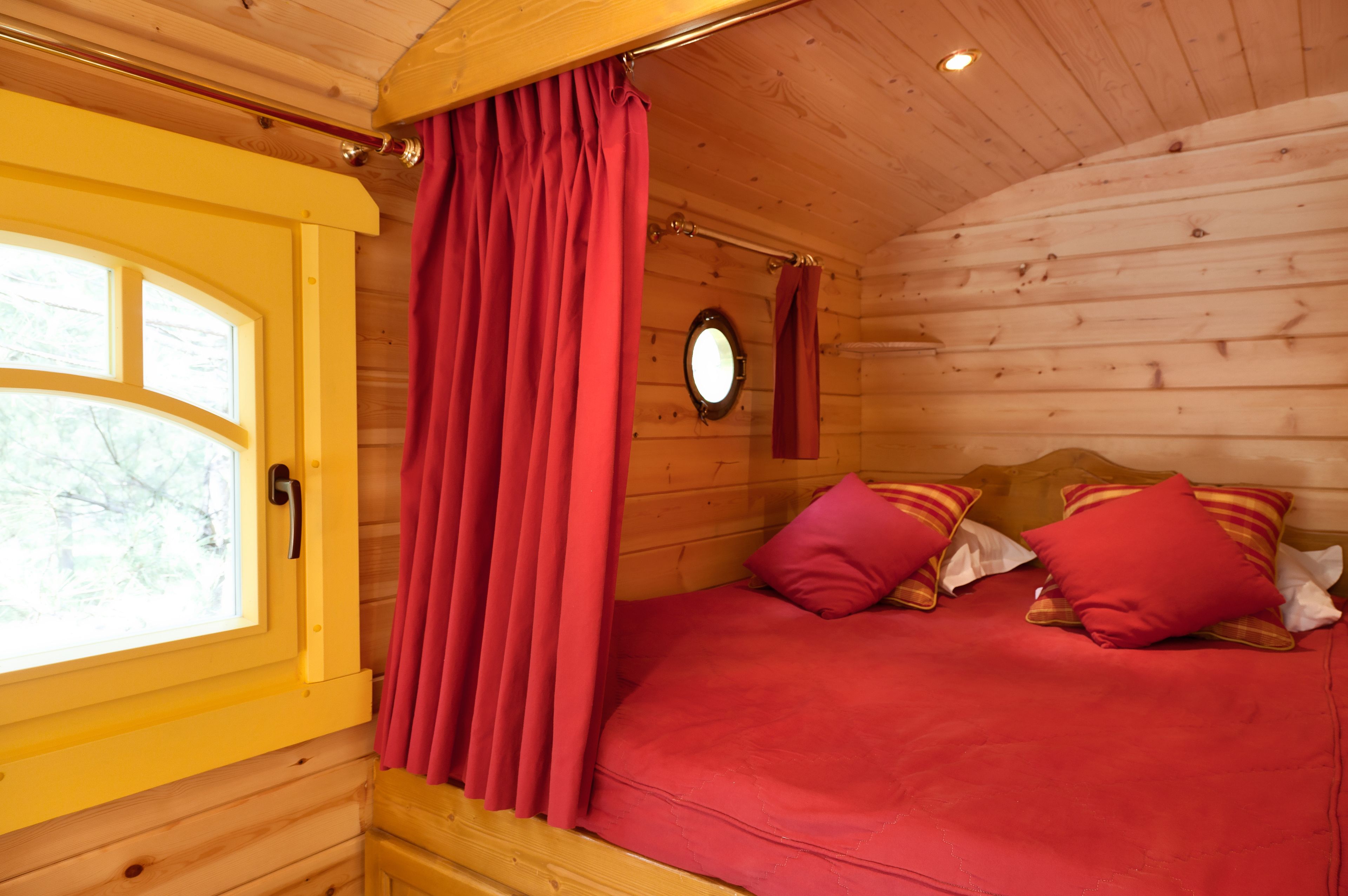 Quarto de cabana de madeira com cama, cortinas vermelhas e uma janela.