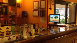 Balcão de recepção de hotel com monitor de computador, certificados emoldurados e folhetos informativos.