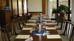 Uma sala de conferências com uma mesa comprida, cadeiras, uma tela de projetor e um vaso de planta.