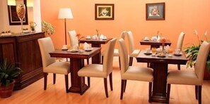 Uma sala de jantar de hotel com mesas e cadeiras de madeira, um buffet e quadros nas paredes.