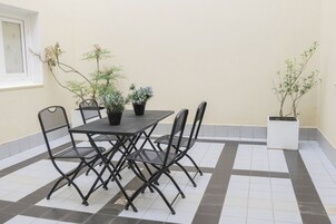Um espaço ao ar livre com mesa, cadeiras, plantas em vasos e piso de azulejos.