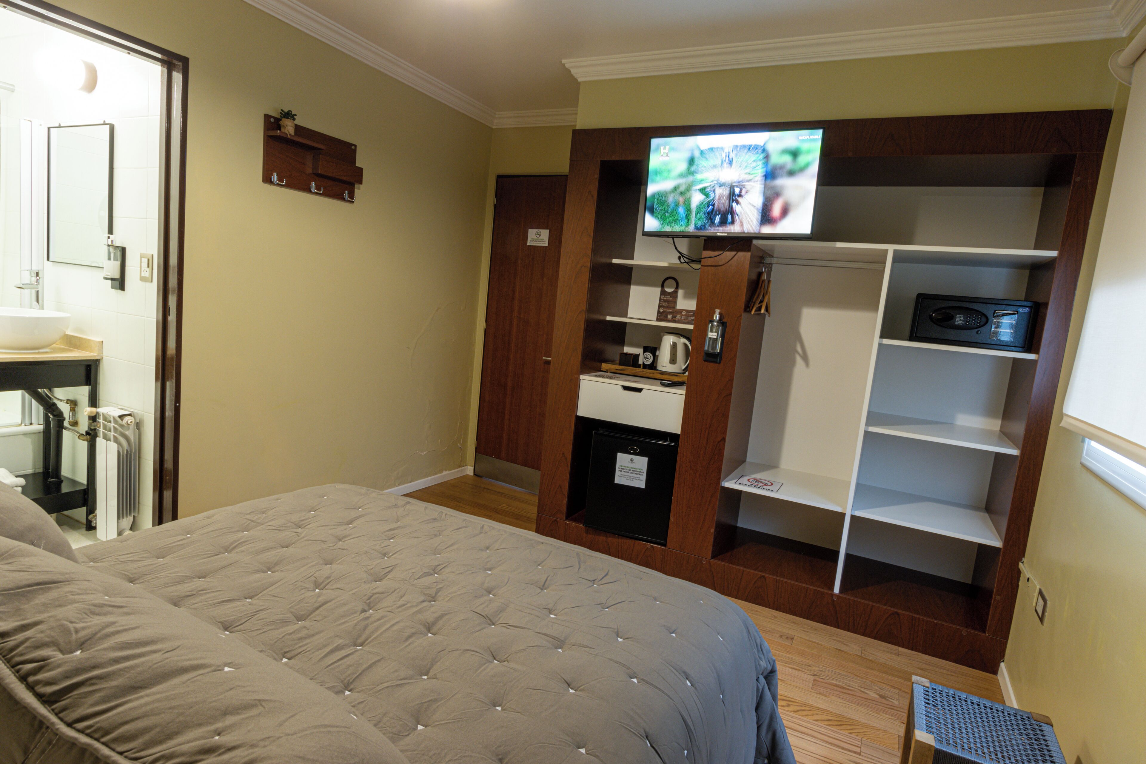 Quarto de hotel com uma cama grande, televisão montada num armário de madeira, pequena cozinha e closet espaçoso.