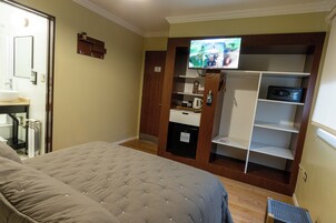 Quarto de hotel com uma cama grande, televisão montada num armário de madeira, pequena cozinha e closet espaçoso.
