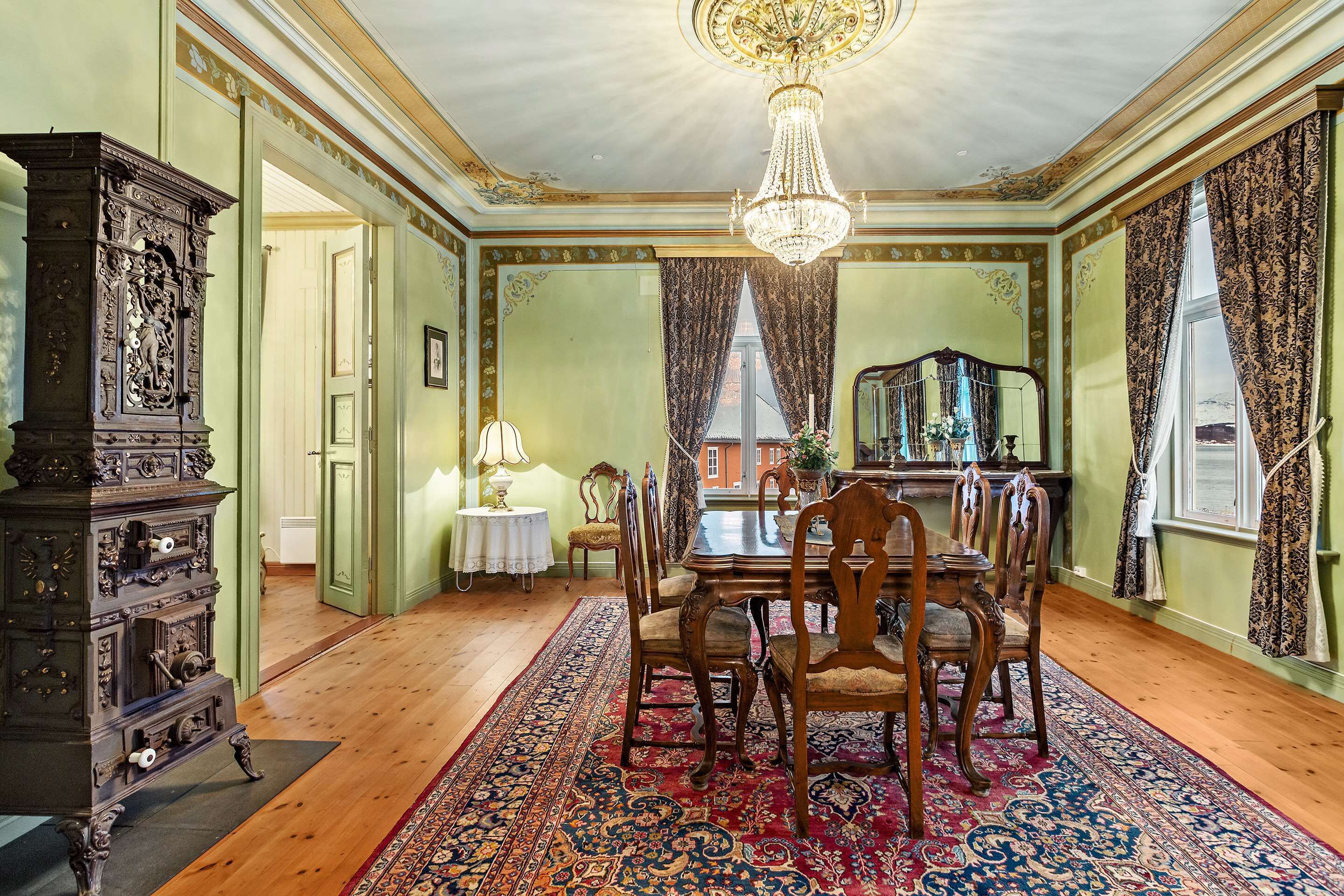 Uma sala de jantar com mesa e cadeiras de madeira, um candelabro e um tapete estampado.