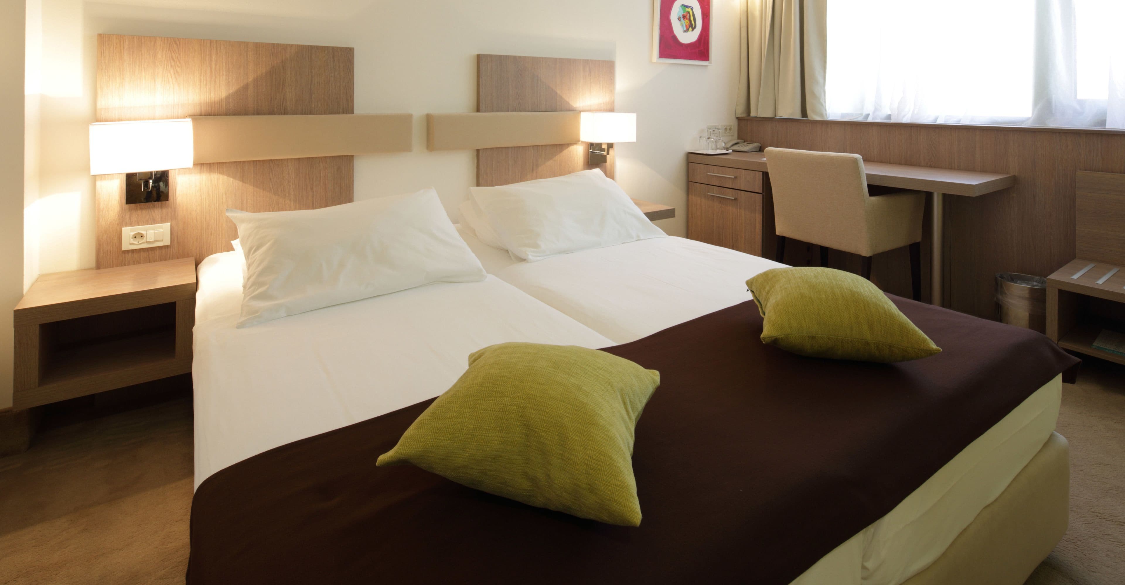 Quarto de hotel com uma cama grande, duas mesas de cabeceira com luminárias, uma escrivaninha e uma cadeira.