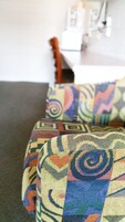Close-up de uma almofada estampada em um sofá, com uma parede branca e uma porta ao fundo.