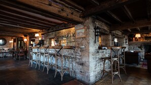 Um espaço de bar rústico, com paredes de pedra, vigas de madeira e banquetas de vime.