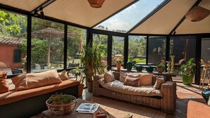 Um quarto amplo com uma janela grande, um sofá, uma mesa de centro e um vaso de planta.