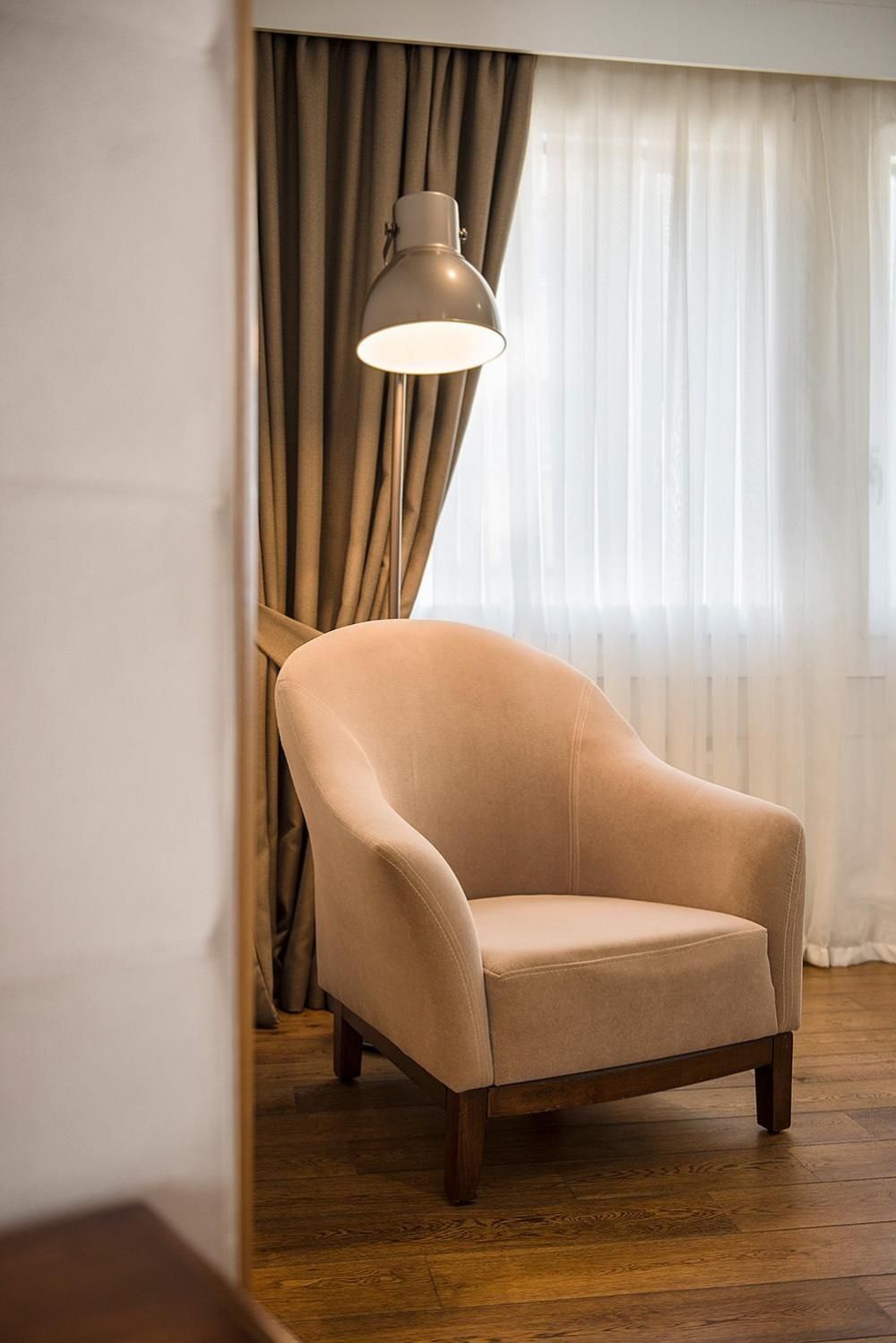 Um quarto com uma poltrona bege, uma luminária de chão e uma janela com cortinas.