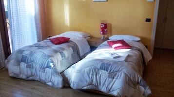 Quarto com duas camas, piso de madeira, luminária vermelha e um quadro na parede.