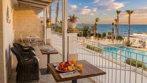 Uma varanda com cadeiras de vime, uma mesa com frutas e suco, e vista para o mar.