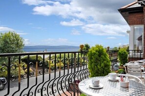 Uma varanda com vista para o mar, uma mesa com xícaras e um edifício com fachada de tijolos.