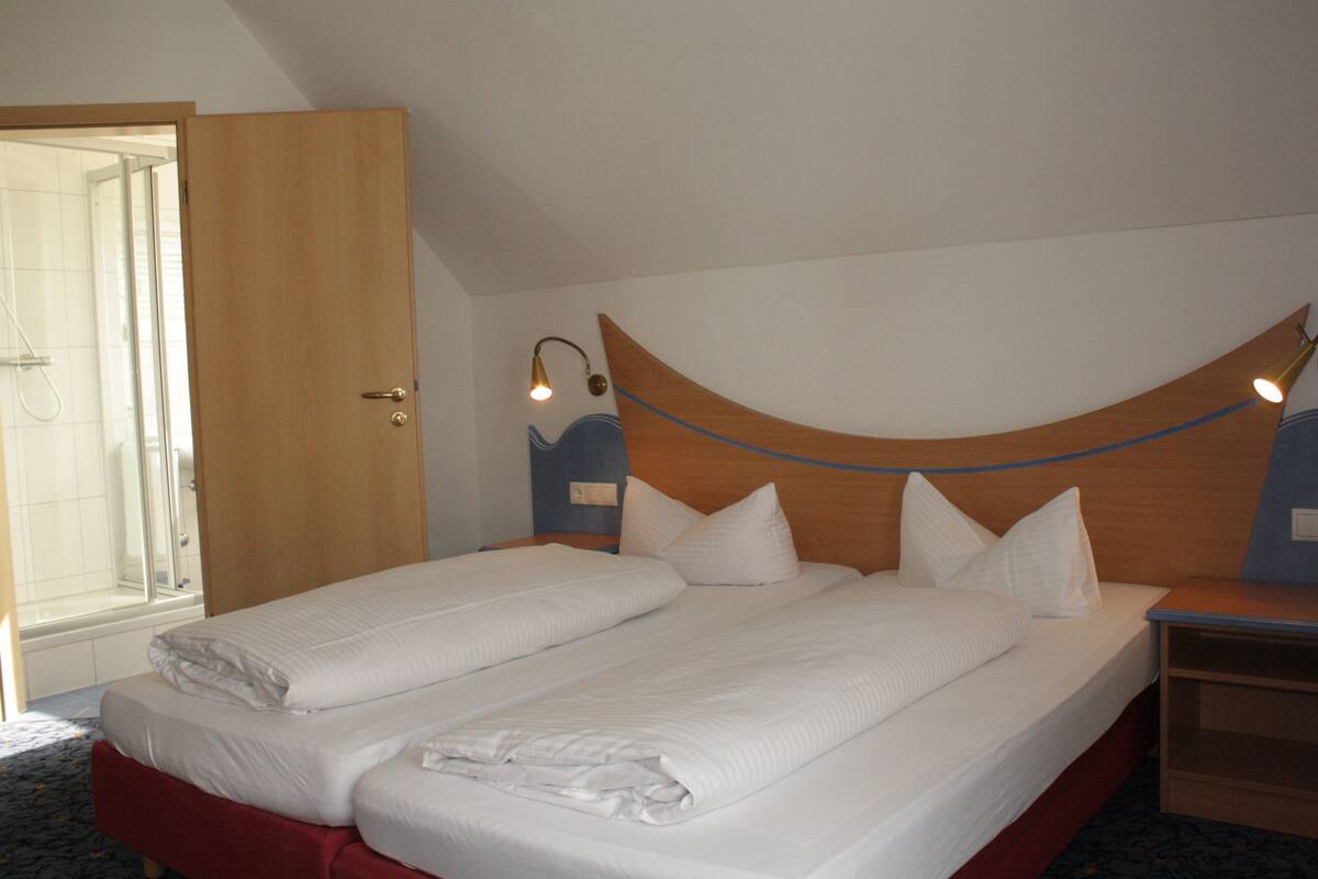 Uma cama de casal com roupa de cama branca, cabeceira de madeira e mesa de cabeceira com abajur.