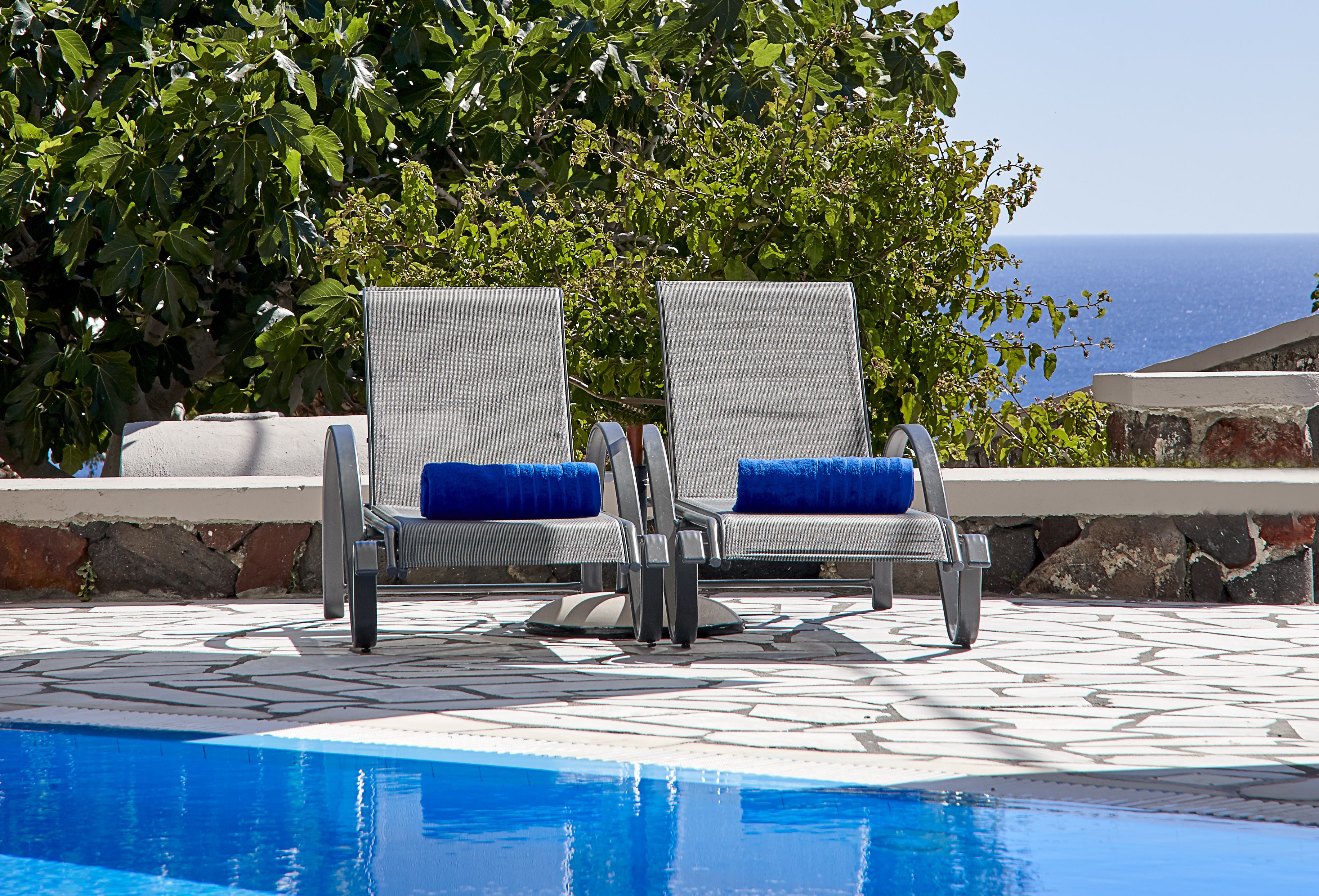 Área da piscina com duas espreguiçadeiras e vista para o mar.