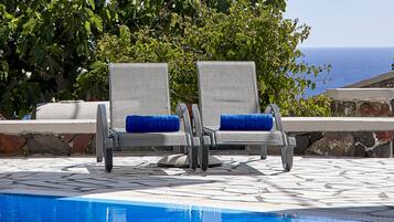 Área da piscina com duas espreguiçadeiras e vista para o mar.