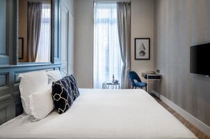 Quarto de hotel com uma cama grande, uma escrivaninha com cadeira, televisão e janela com cortinas.