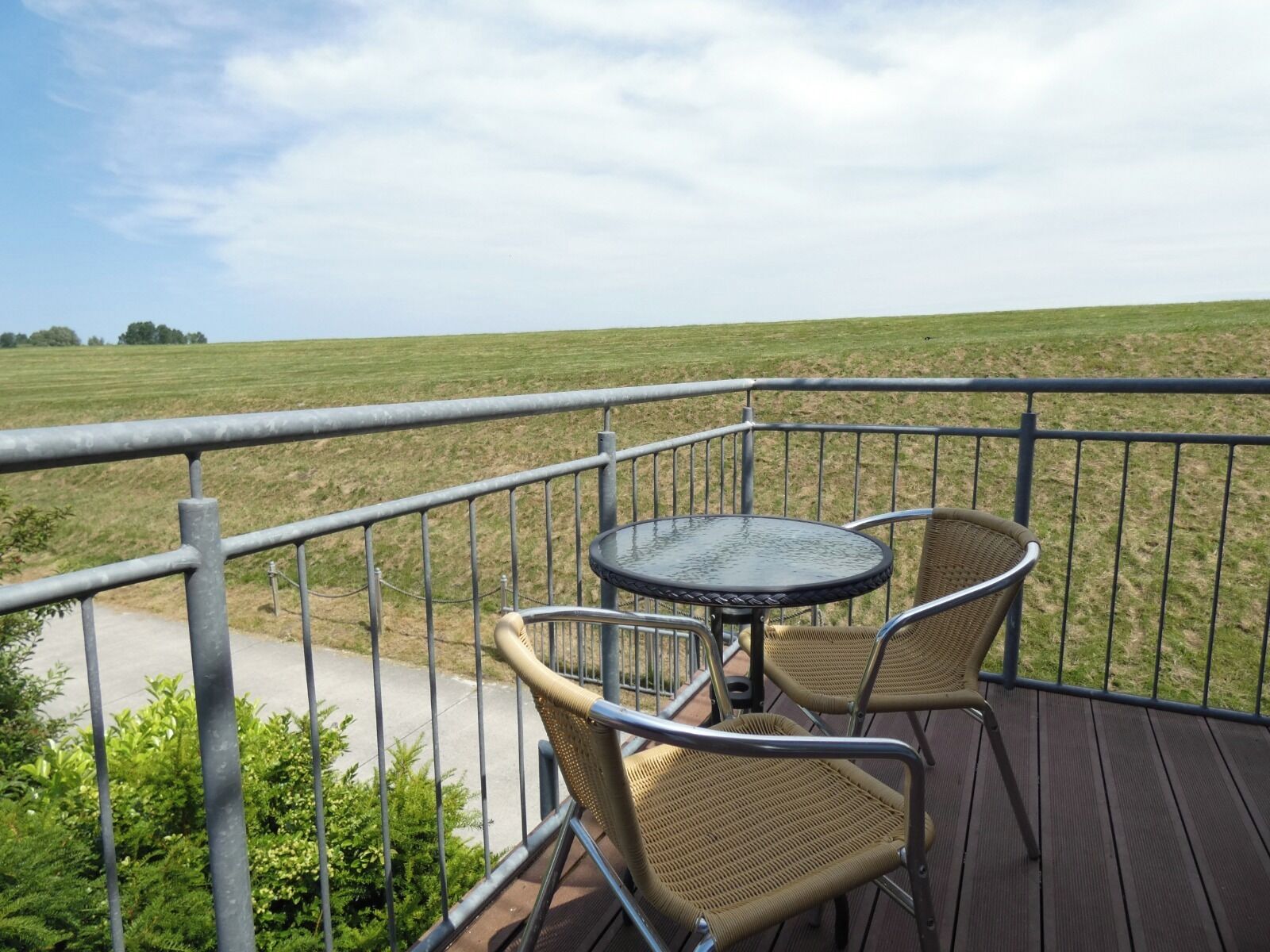Varanda com mesa e duas cadeiras de vime, com vista para um campo gramado.