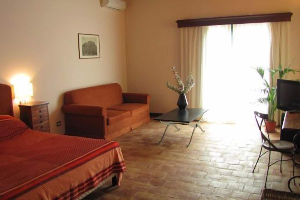 Quarto de hotel com uma cama, um sofá, uma mesinha de centro e uma televisão.