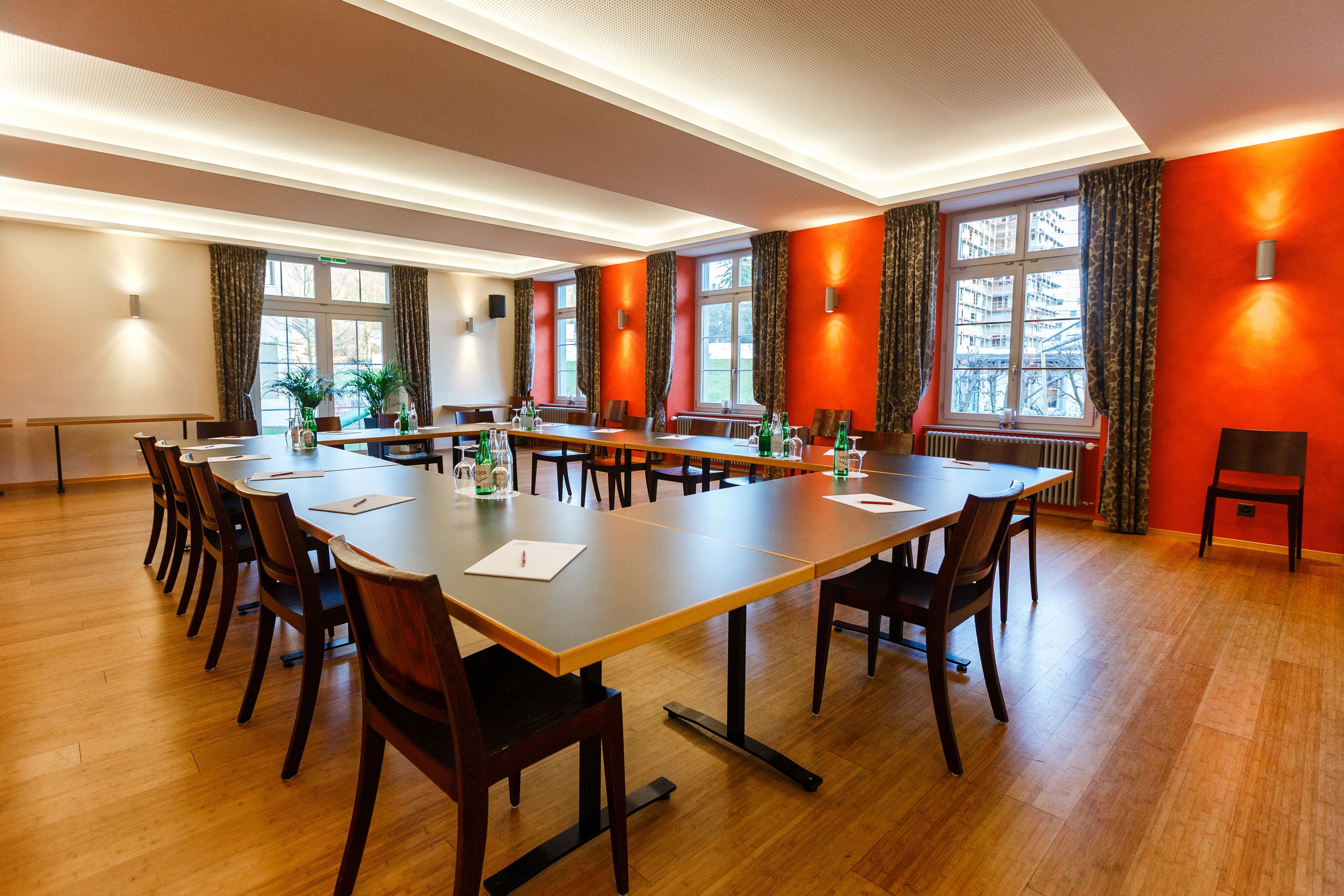 Uma sala de conferência com uma mesa comprida, várias cadeiras e amplas janelas com cortinas.