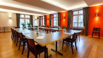 Uma sala de conferência com uma mesa comprida, várias cadeiras e amplas janelas com cortinas.