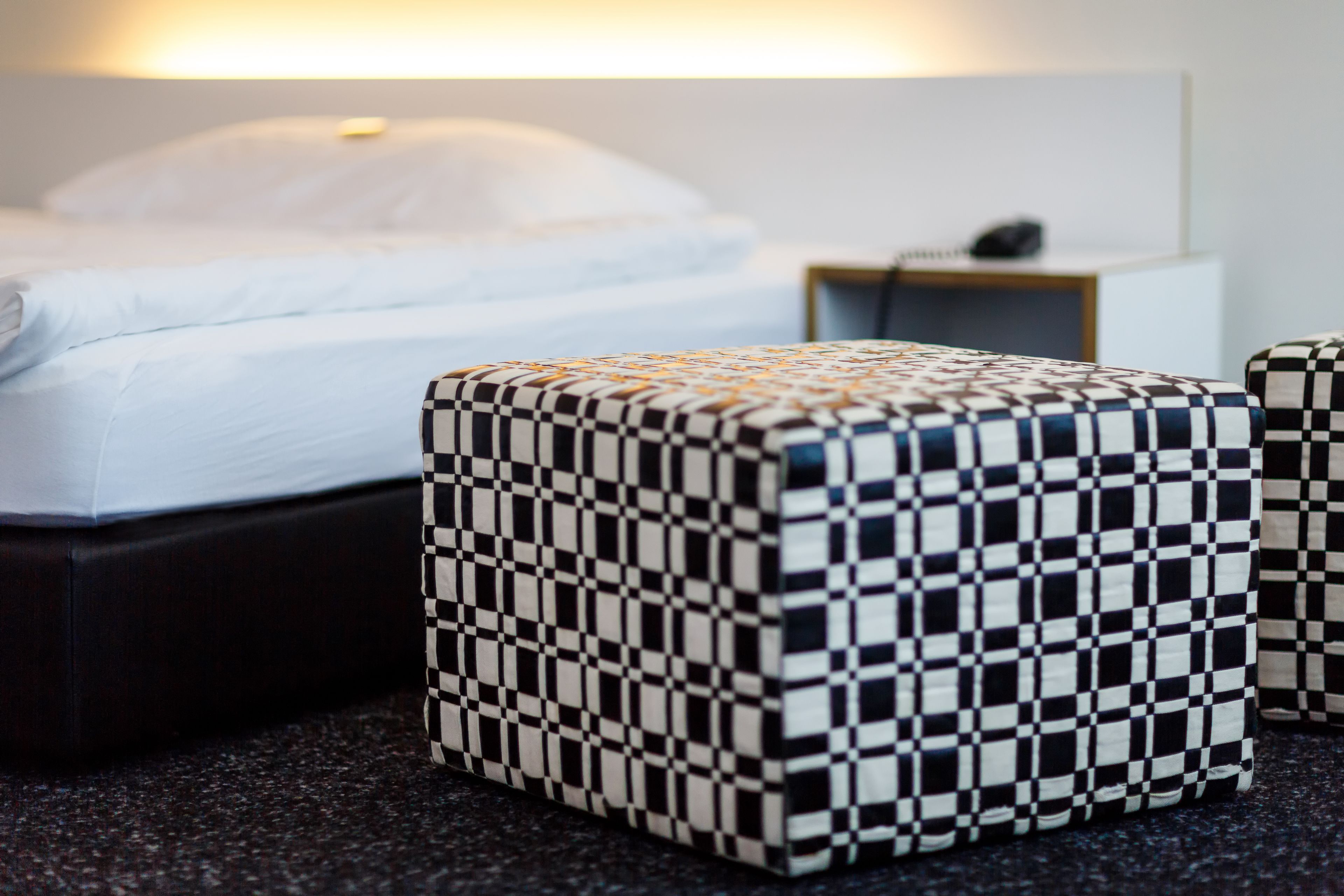 Quarto de hotel com cama, mesa de cabeceira e dois pufes estampados em xadrez.