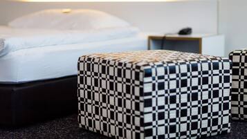 Quarto de hotel com cama, mesa de cabeceira e dois pufes estampados em xadrez.