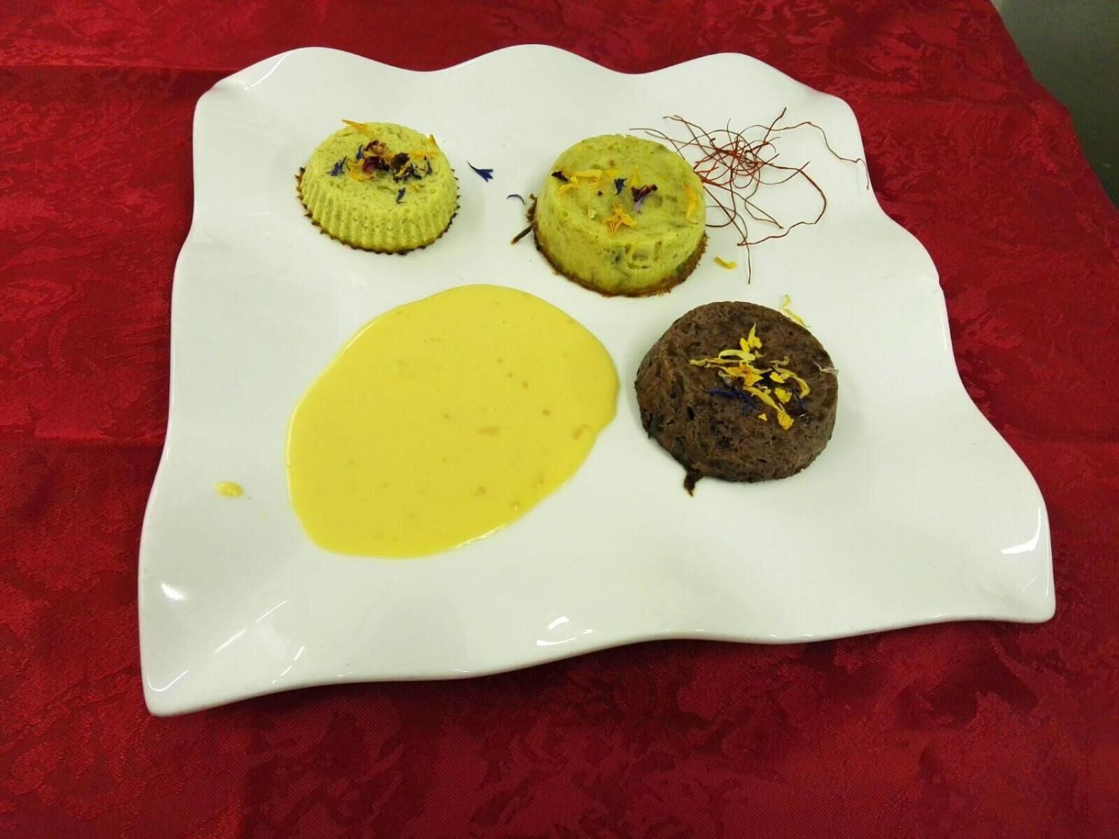Um prato branco com três tipos diferentes de comida e molho amarelo sobre uma toalha de mesa vermelha.