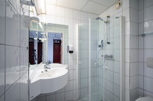 Casa de banho moderna com cabine de duche envidraçada, lavatório branco e um espelho grande.
