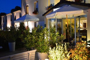 Área externa bem iluminada, com plantas em vasos e guarda-sóis, transmitindo a sensação de um pátio ou jardim.