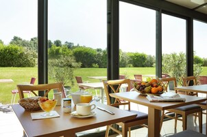Disposição para o café da manhã, com uma mesa, cadeiras e vista para uma paisagem verde através de grandes janelas.