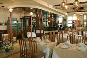 Restaurante com mesas postas para refeições, área de bar e cozinha ao fundo.