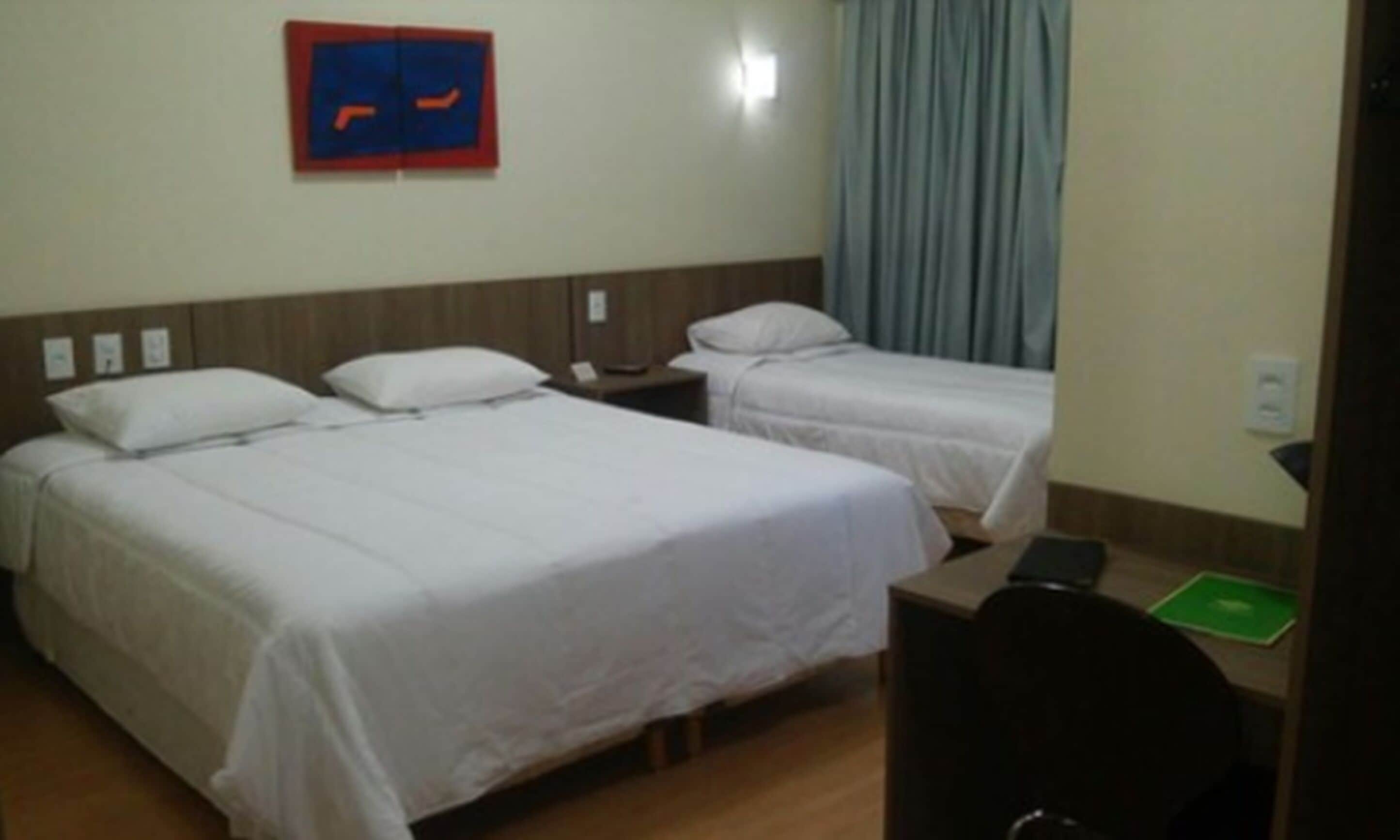 Quarto de hotel com duas camas, uma escrivaninha e uma cadeira.
