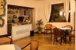 Uma área de refeições acolhedora com cadeiras de madeira e uma mesa, um balcão com garrafas e uma planta em vaso.