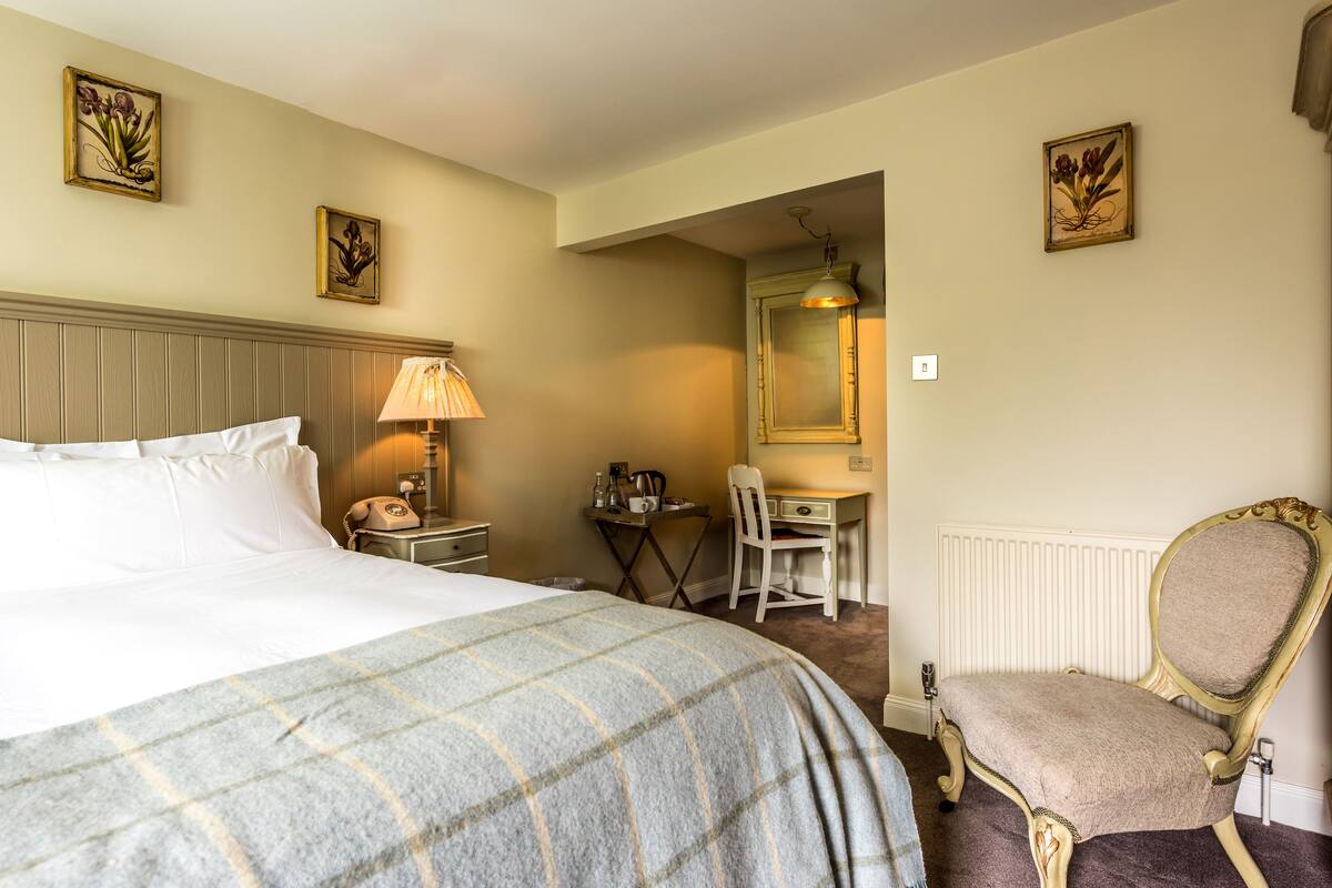 Quarto de hotel com cama, escrivaninha, cadeira e luminária.
