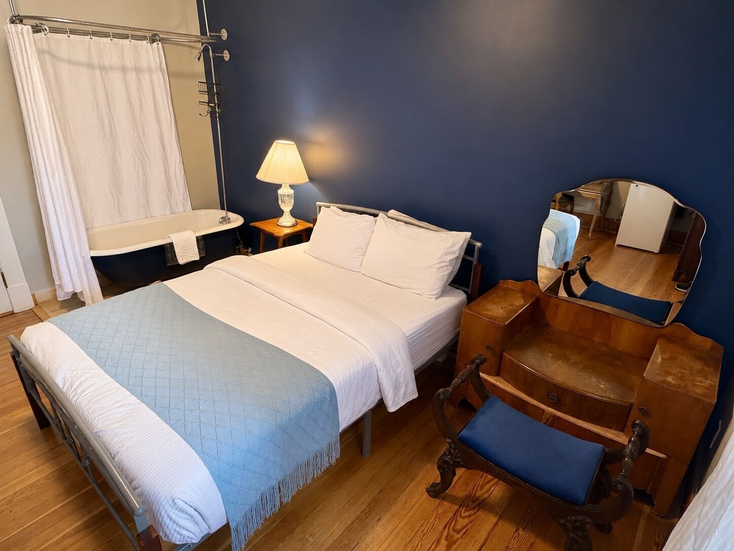 Um quarto com cama, mesa de cabeceira, luminária, cadeira e espelho.