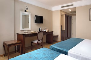 Quarto de hotel com escrivaninha, cadeira, duas camas, televisão e espelho.