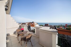 Varanda com cadeiras de vime e uma mesa, com vista para a paisagem urbana costeira.
