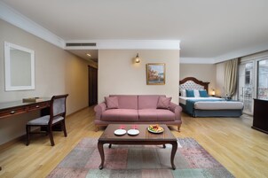 Um quarto com sofá rosa, uma secretária de madeira, uma mesa de jantar com pratos e uma fruteira, uma cama com roupa de cama azul e um quadro na parede.