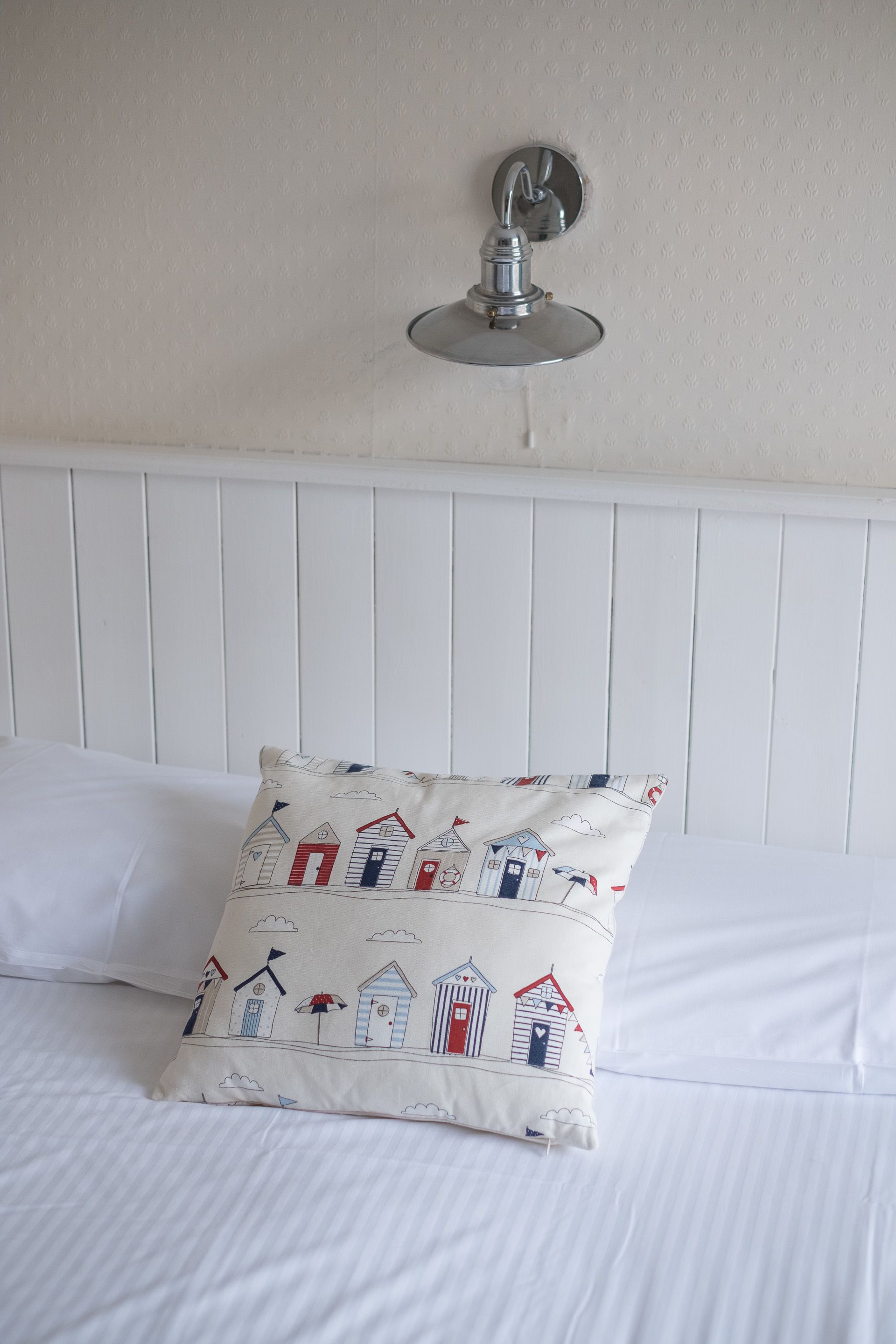 Cama bem arrumada com roupa de cama branca e almofada com padrão de vila à beira-mar.