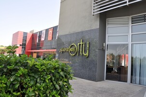 Entrada de hotel com fachada moderna, uma grande porta de vidro e uma placa com o nome do hotel.