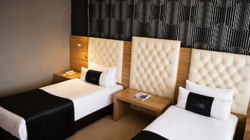 Quarto de hotel com duas camas, uma cabeceira de madeira, uma mesa de cabeceira com telefone e uma parede com textura.