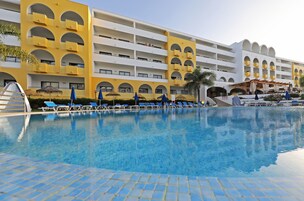 Hotel com uma piscina grande, cadeiras de descanso azuis e varandas amarelas.