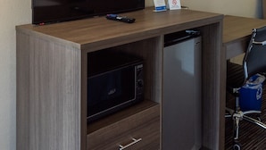 Quarto de hotel com televisão de tela plana, mini-geladeira, micro-ondas e um pequeno armário com gavetas.