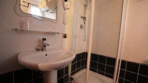 Casa de banho com lavatório branco, espelho, secador de cabelo e chuveiro.