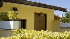 Um edifício com fachada amarela, porta marrom e uma pequena varanda com guarda-corpo branco.