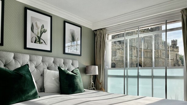 Quarto com cama grande, cabeceira estofada e vista para edifícios históricos através de uma janela ampla.